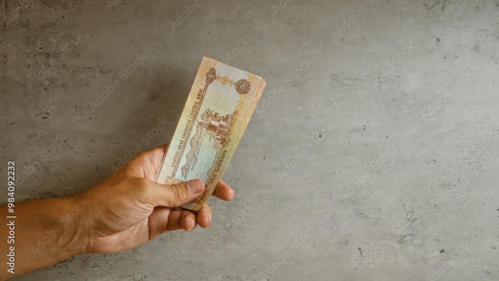 Hand holding uae dirhams against a concrete background, showcasing ...