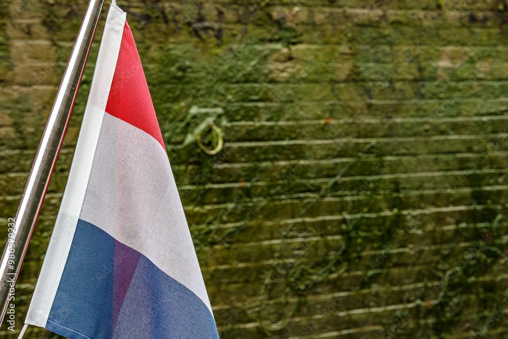 Dutch flag on flagpole at stern of a ship against brick wall with moss ...