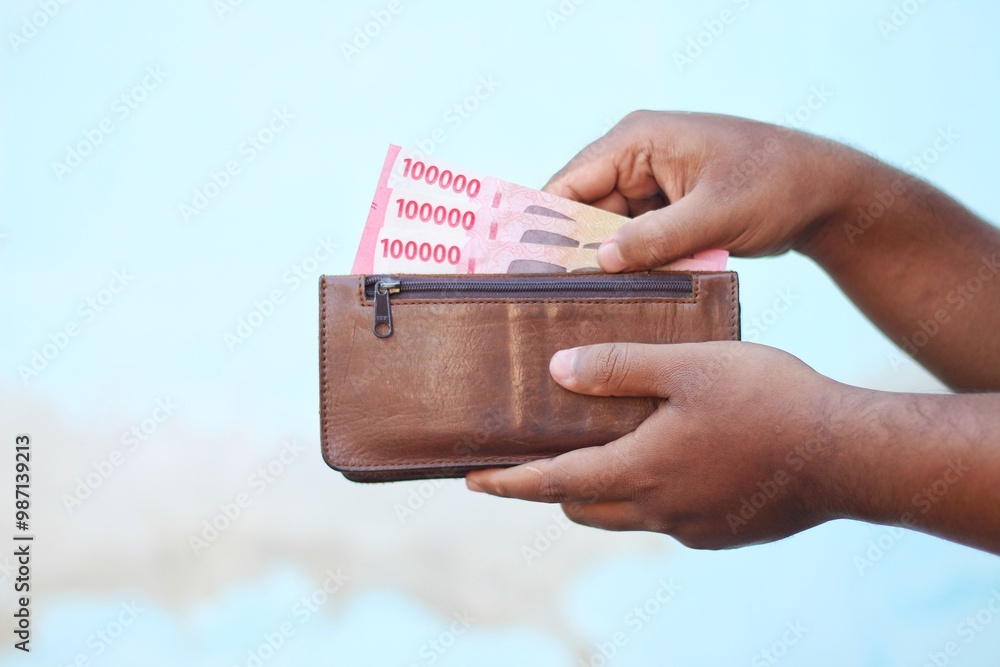 Hand holding a wallet containing several Indonesian rupiah notes. The ...