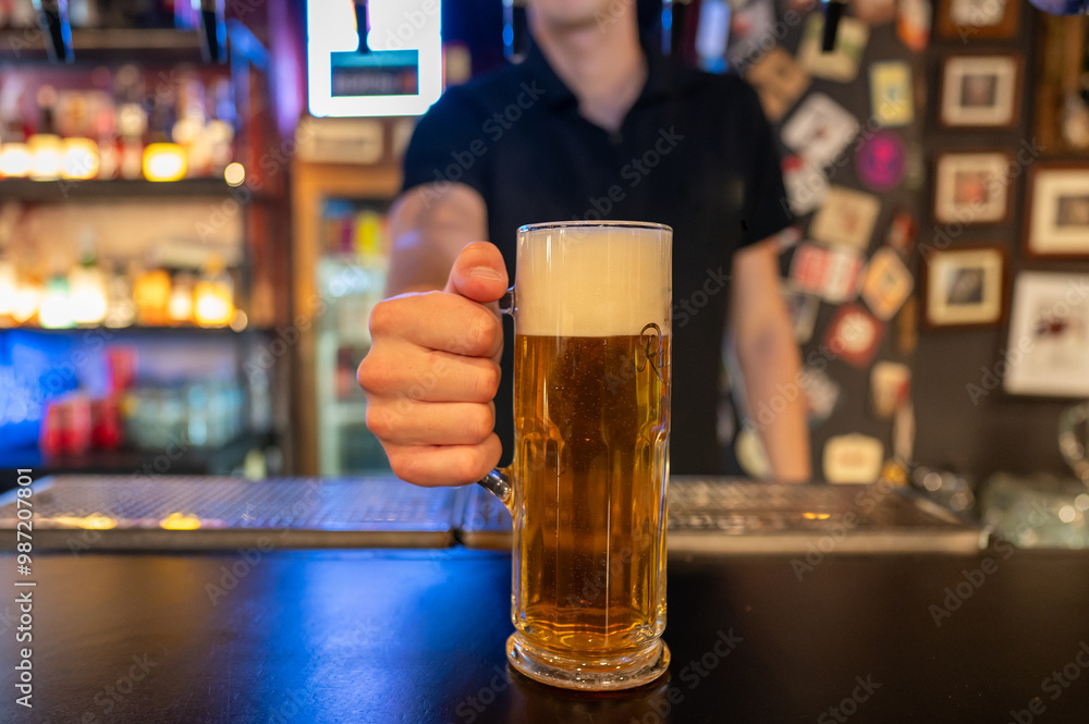 A person holding a full pint of beer with a foamy head, standing behind ...