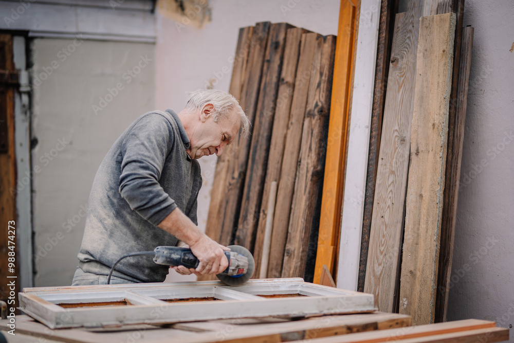 An elderly man is sanding a wooden window frame using a power tool in a ...
