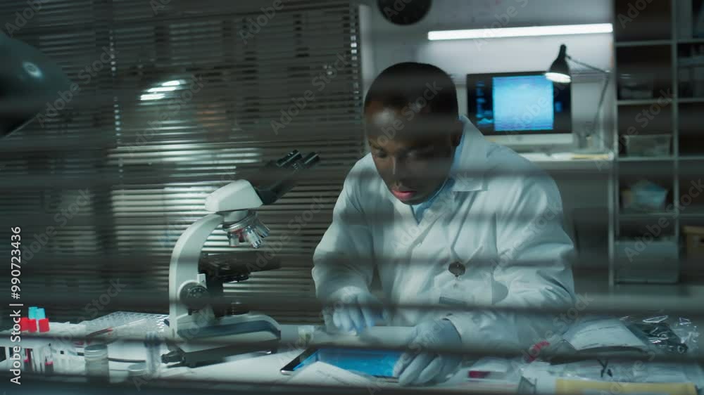 View though window blinds of African American scientist studying ...
