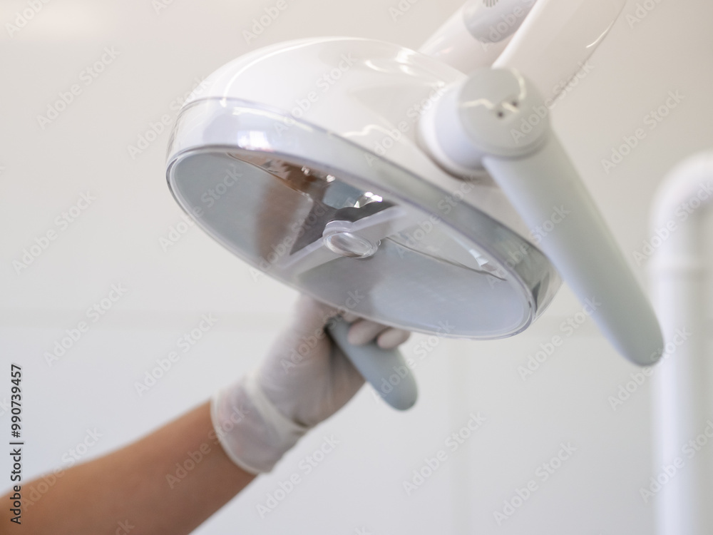 A dental professional adjusts a lamp overhead while preparing for a ...