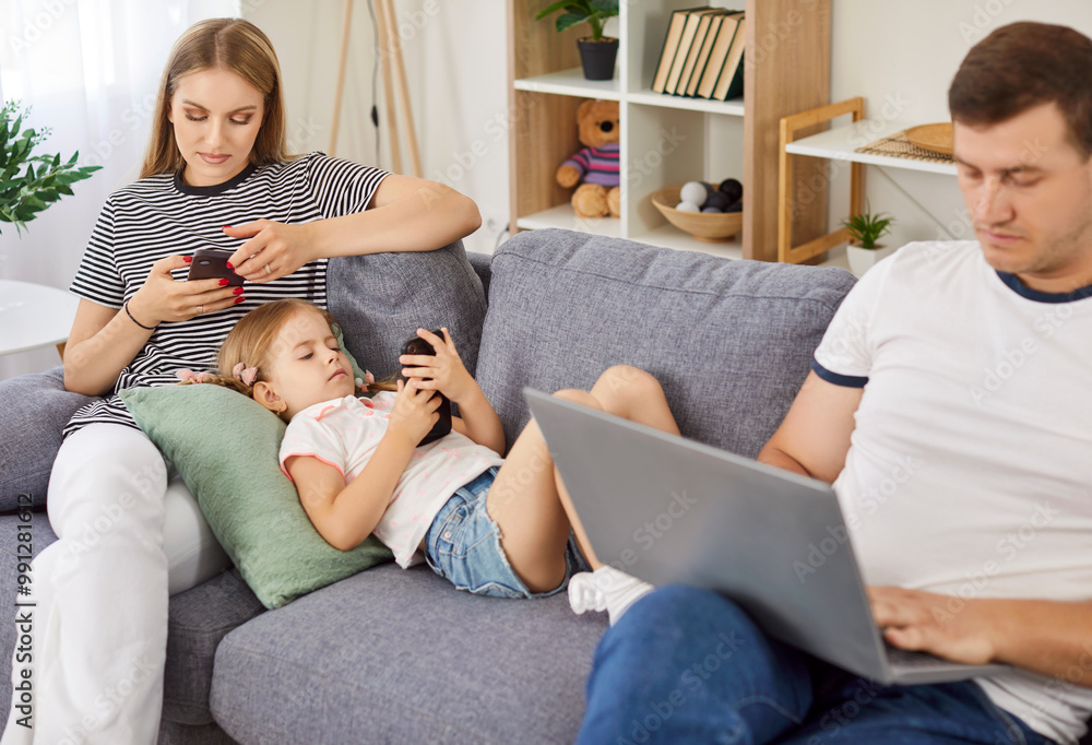 Family at home using laptop and smartphones sitting on sofa, entertaining online obsessed with ...