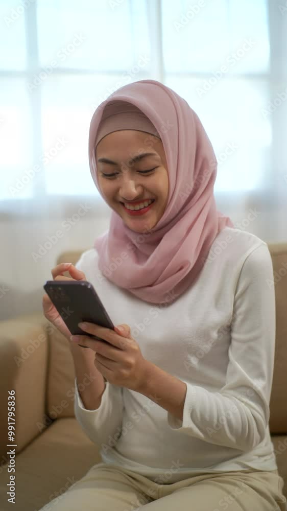 Vertical of young cheerful muslim woman in hijab checking social media ...