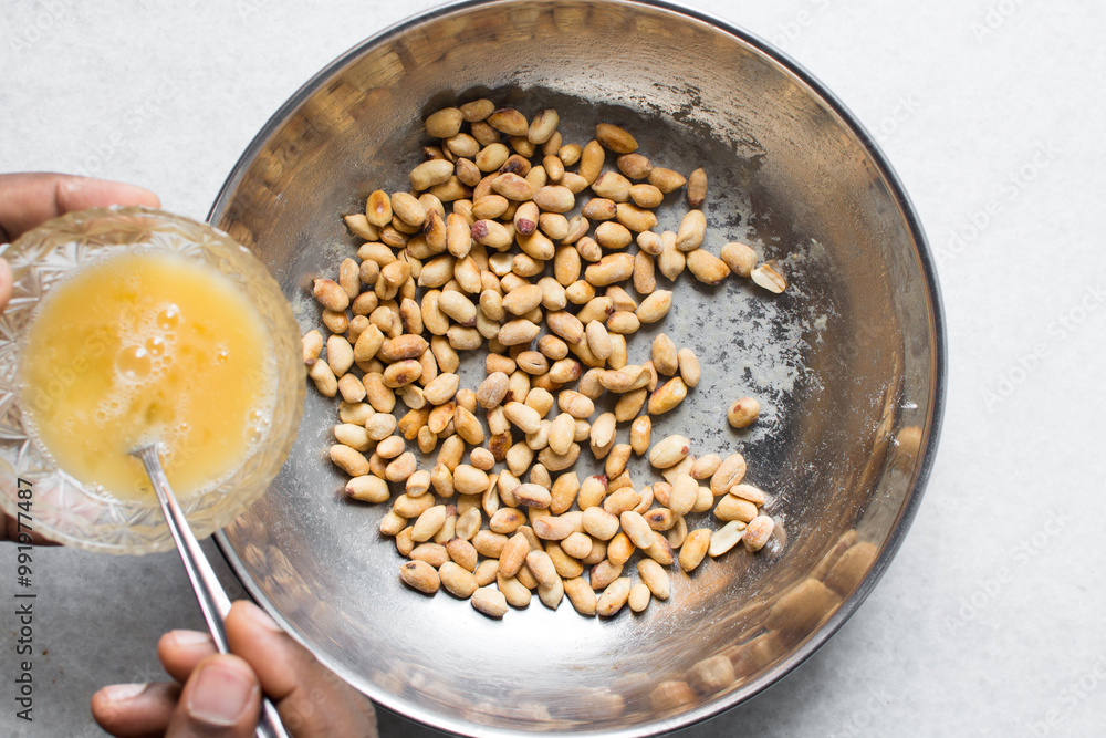 Overhead view of roasted peanuts being coated with egg and flour in a ...