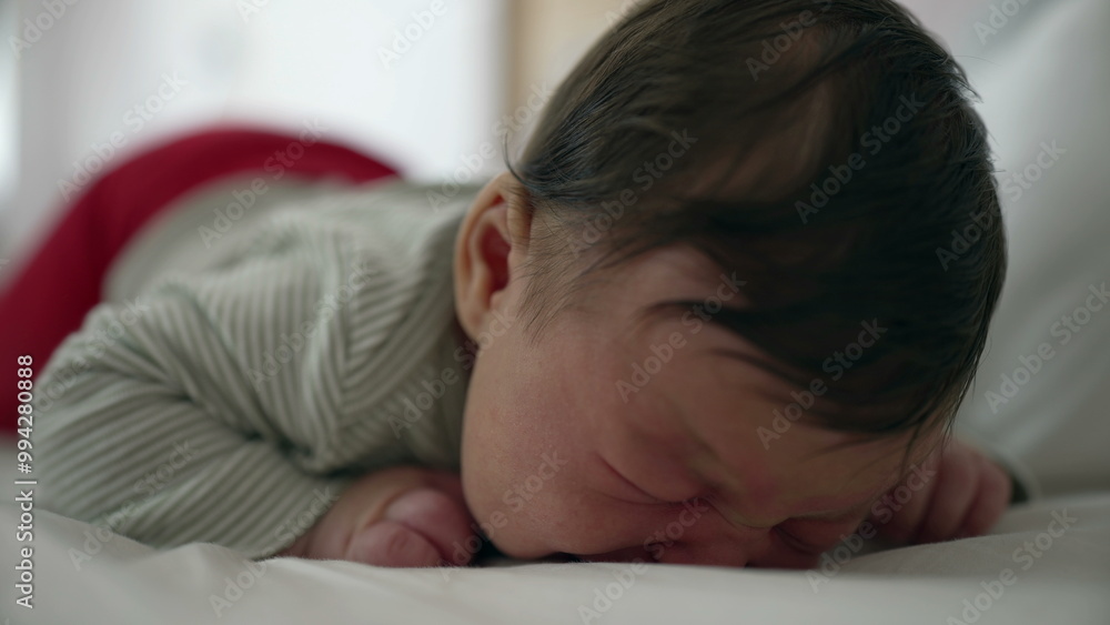 Newborn baby crying while lying face down on a bed, dressed in a ...