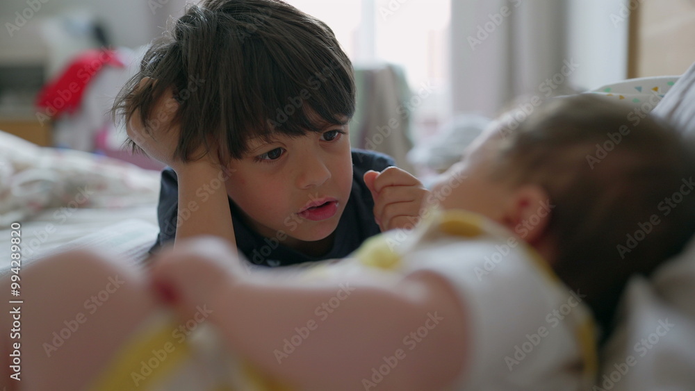 Older sibling lying on a bed, gazing intently at their baby sibling ...