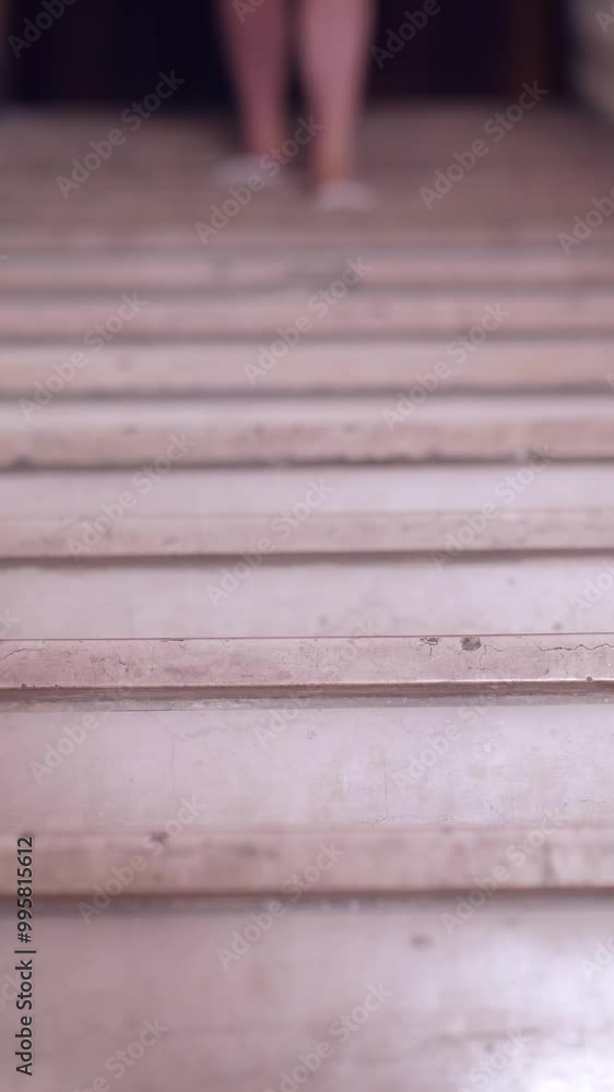 Vertical. A woman's legs are seen descending a long staircase inside a ...