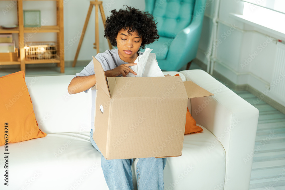 African girl unpacking delivery looking in box. Happy woman opening ...