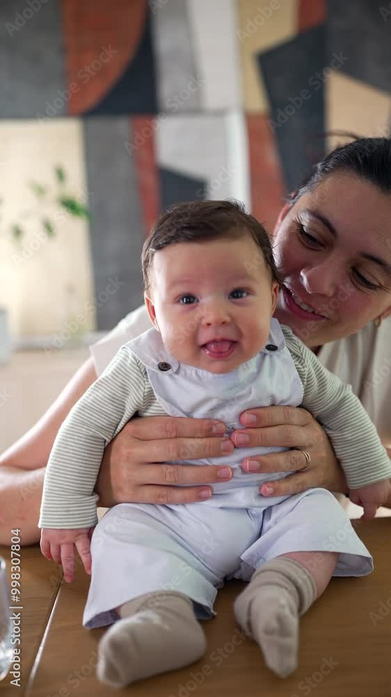Baby sitting on a table, supported by the mother from behind. baby ...