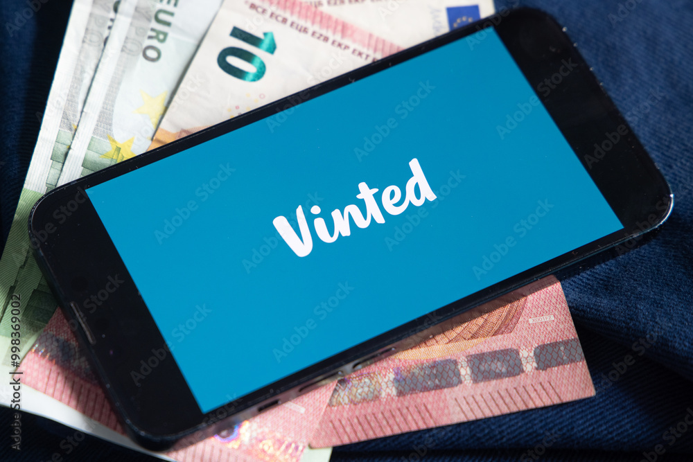 Iphone with Vinted logo on screen on stack of money. Vinted is a ...