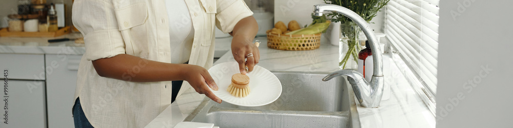 Person washing dishes using a brush in a bright, modern kitchen setting ...