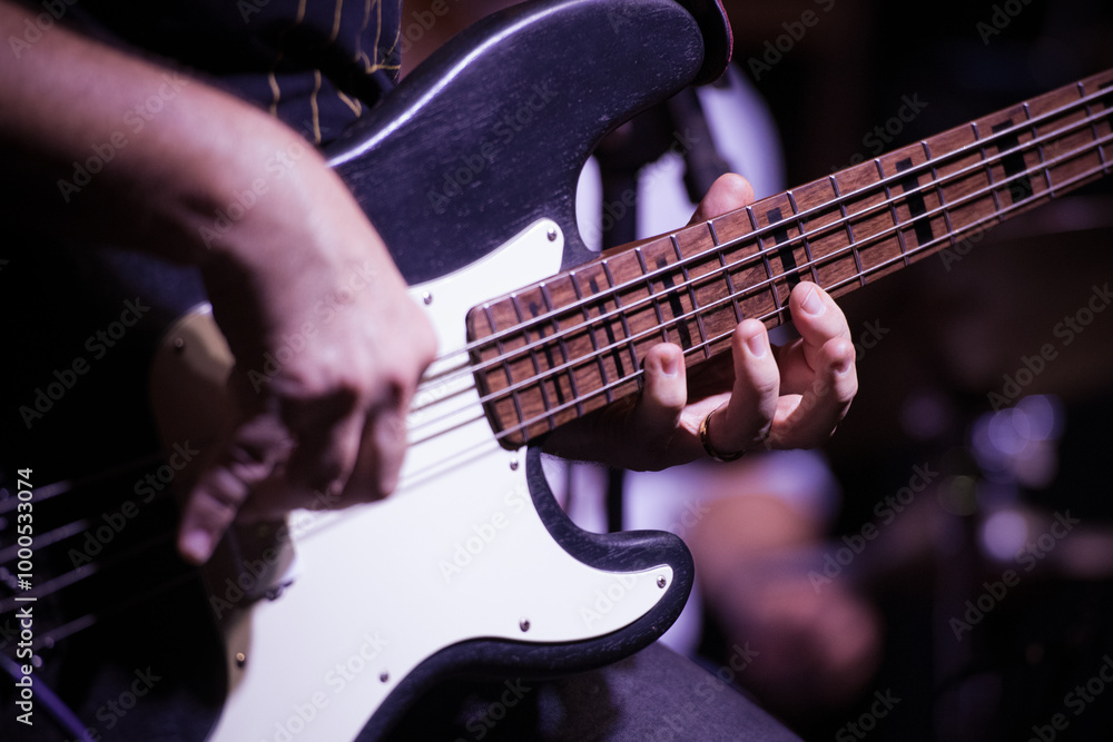 Close-up of a hand playing a bass guitar, strings and fingers in focus ...