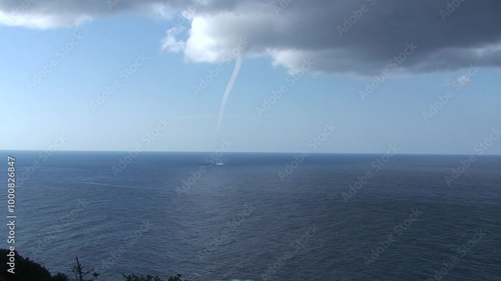 A wide shot of a fully formed waterspout, stretching from the ocean ...