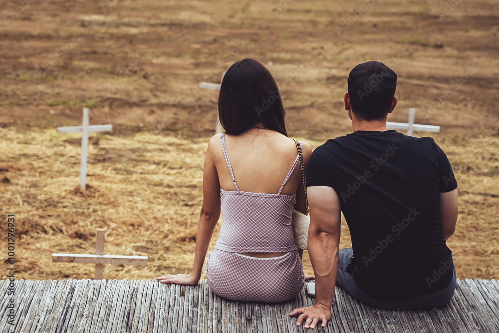 Sad couple sits and mourns the dead with blurred image of cemetery with ...