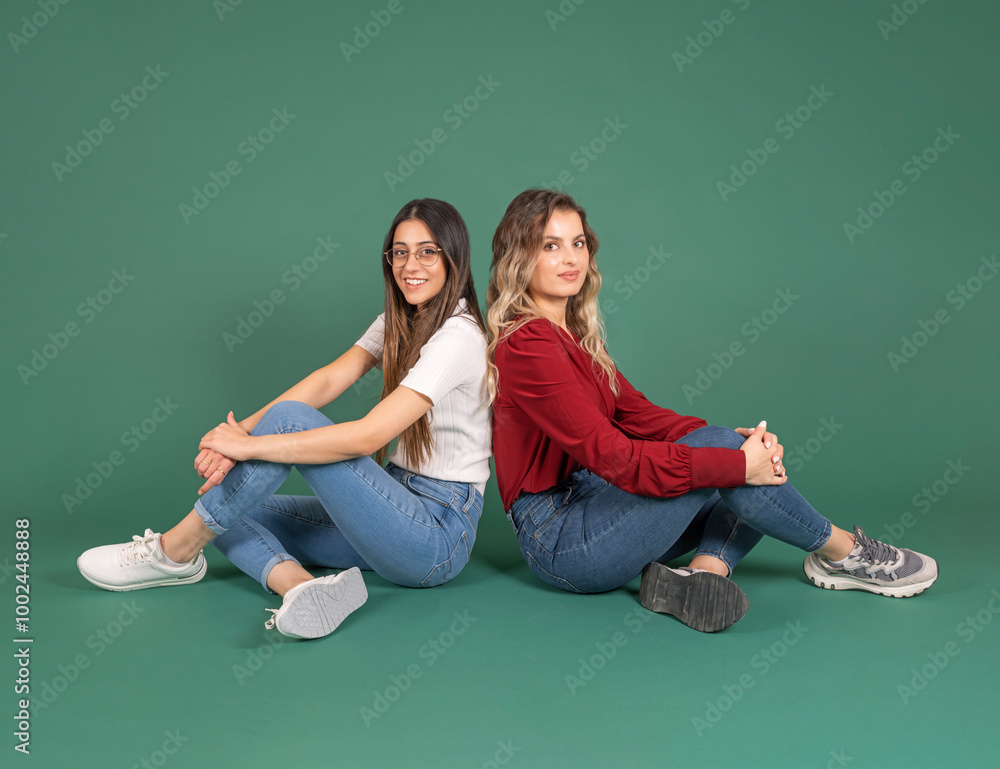 Sitting back to back, two full body beautiful caucasian women girl ...
