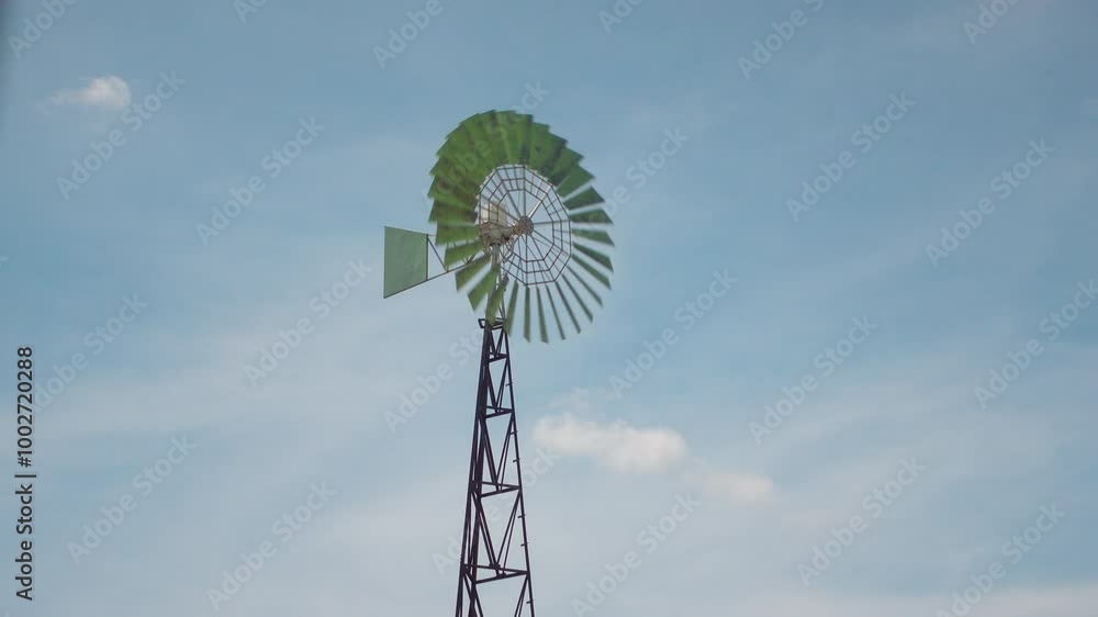 Vintage green windmill with rotating blades against a blue sky with ...