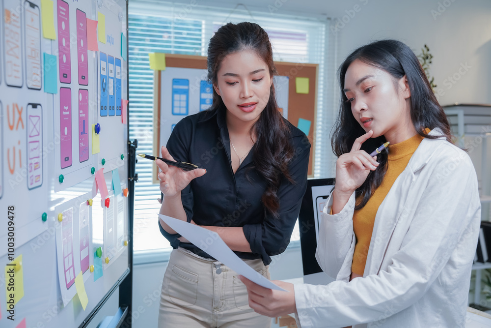 Two Asian Ui Ux Designers Are Discussing Over Mobile App Interface Wireframe Design Displayed On