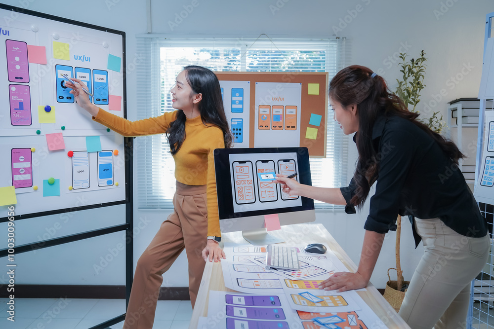 Two Asian Ui Ux Designers Are Working Together In The Office Discussing Mobile App Interface