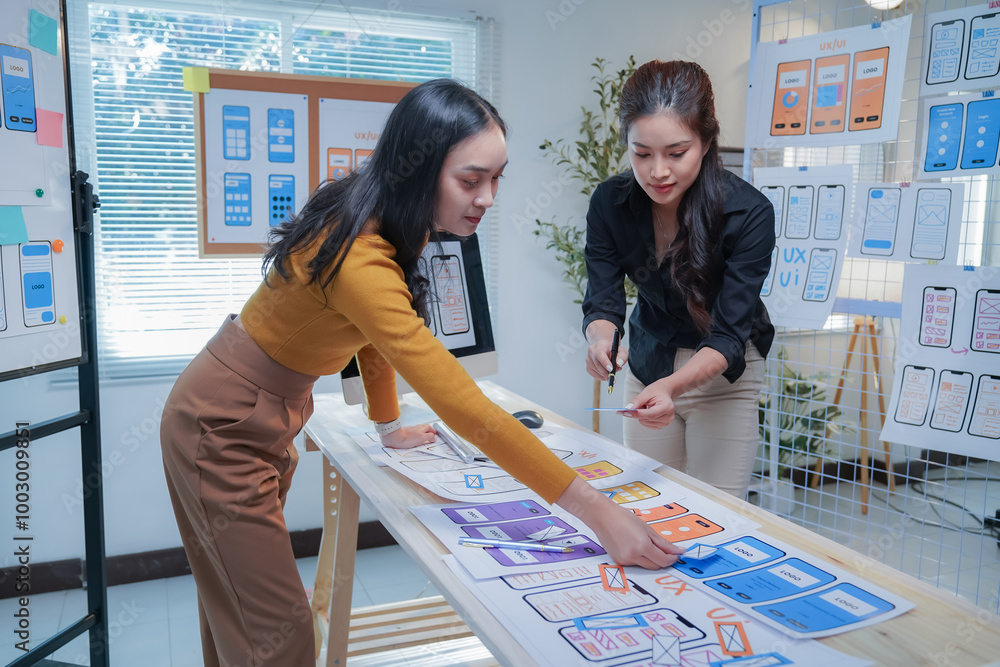 Two female ui/ux designers are working together in an office ...