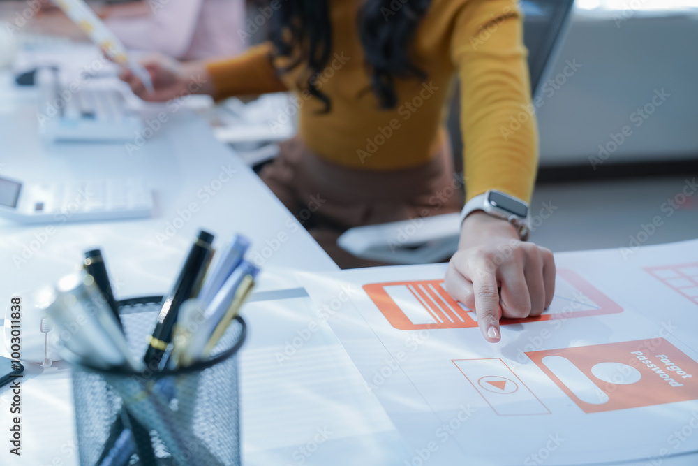Ux ui designer points at a mobile app wireframe in a busy office ...