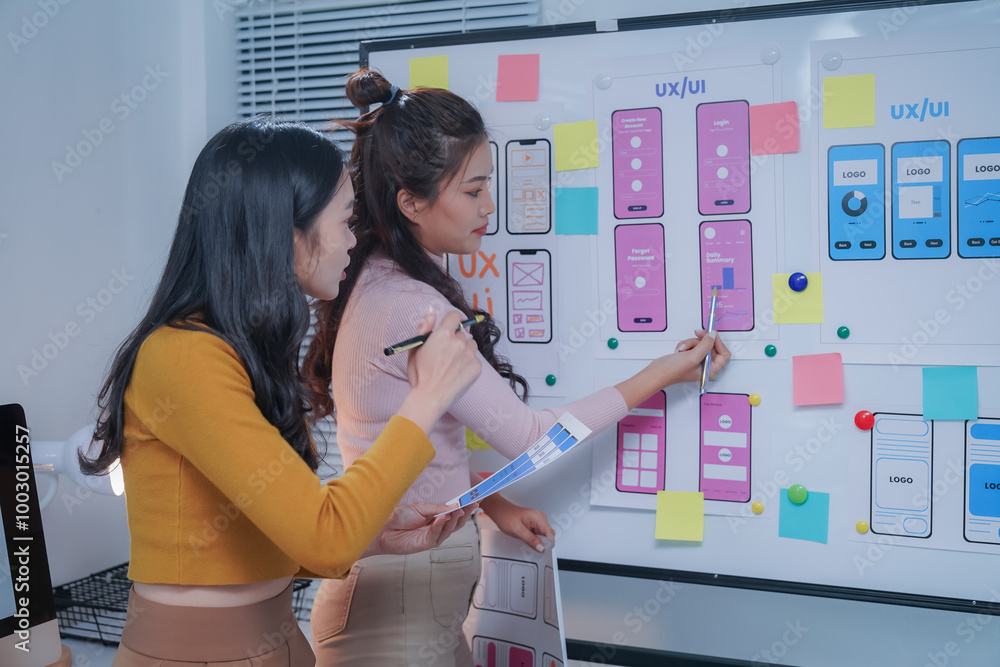 Two asian female ui/ux designers are discussing about mobile app ...