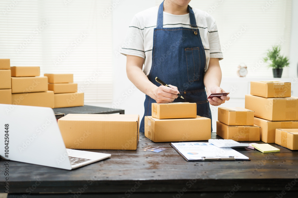 A man is working at his desk, preparing parcel boxes for shipment. He ...