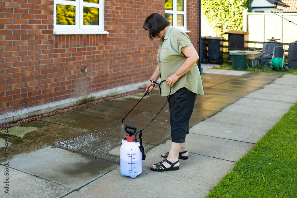 Woman spraying gray concrete patio paving slabs with liquid weed killer ...