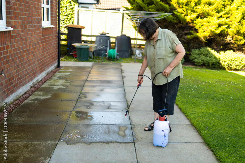 Woman spraying gray concrete patio paving slabs with liquid weed killer ...