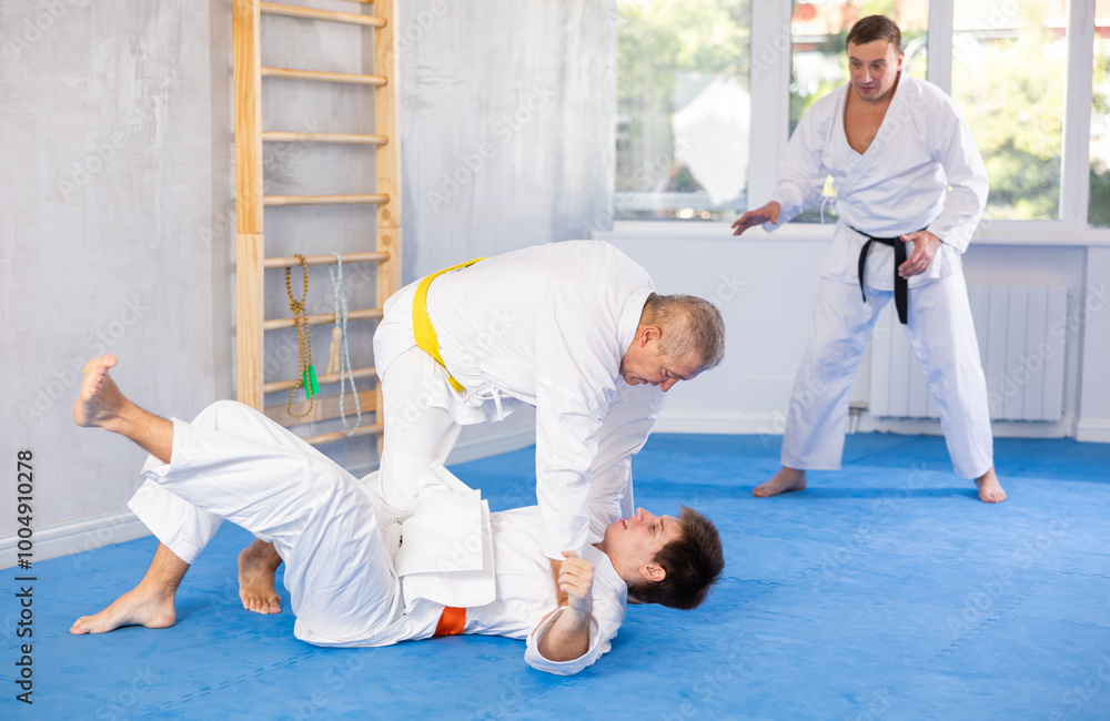 Experienced elderly male karate instructor demonstrating attacking techniques in sparring with ...
