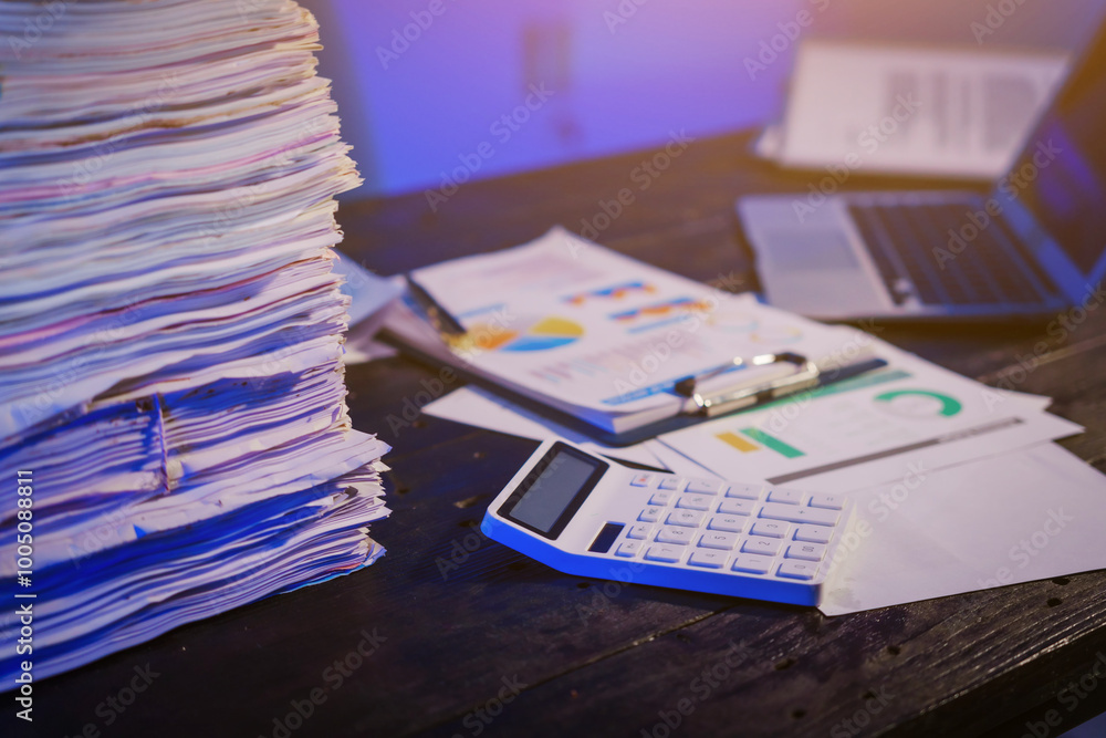 stack of papers rests on a black wooden desk in a dimly lit office room ...