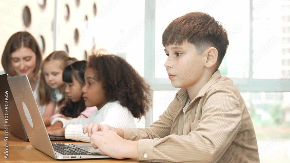 Boy playing laptop with multicultural friend learning prompt at STEM technology class ...