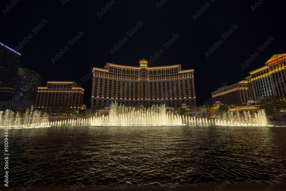 Fountains of Bellagio lit up during night with iconic Bellagio Hotel in ...