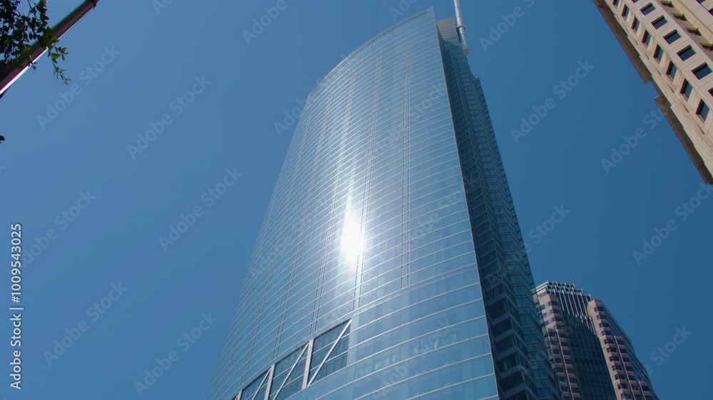 A modern skyscraper with a glass facade reflecting sunlight, set against a clear blue sky. Hi ...