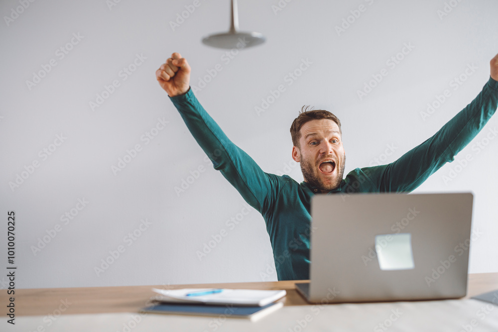 Excited man full of energy sitting behind laptop with big smile on his ...