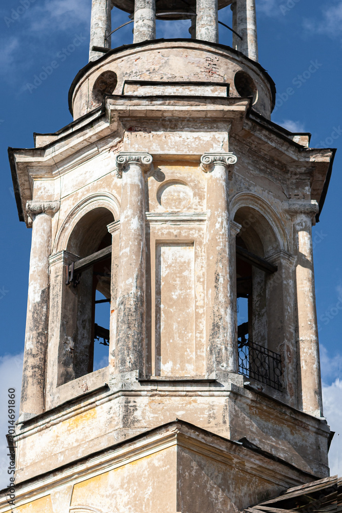 This image shows an old, weathered bell tower with a rusted spire atop ...