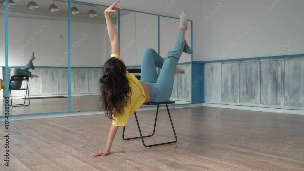 A young female dancer performs smooth dance moves lying on a chair ...