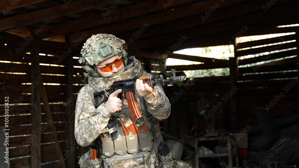 A soldier in full combat gear aims his assault rifle while taking cover ...