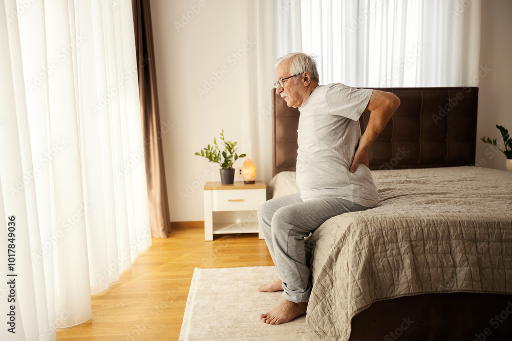 Senior man with backache trying to get up from the bed in the morning ...