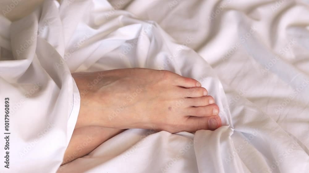 Female legs in bed on white sheets close-up. Female feet. Bare feet of ...