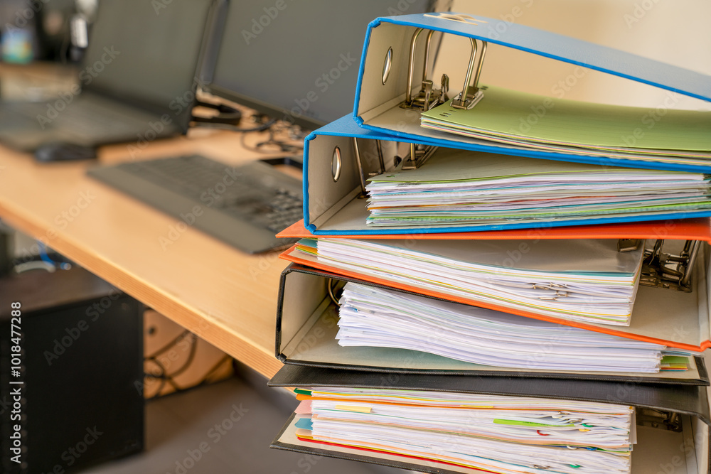 Pile of file folders stacked on desk, in front of computer and laptop ...