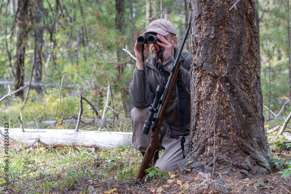 Hunter hiding behind a tree, watching the surroundings with binoculars ...
