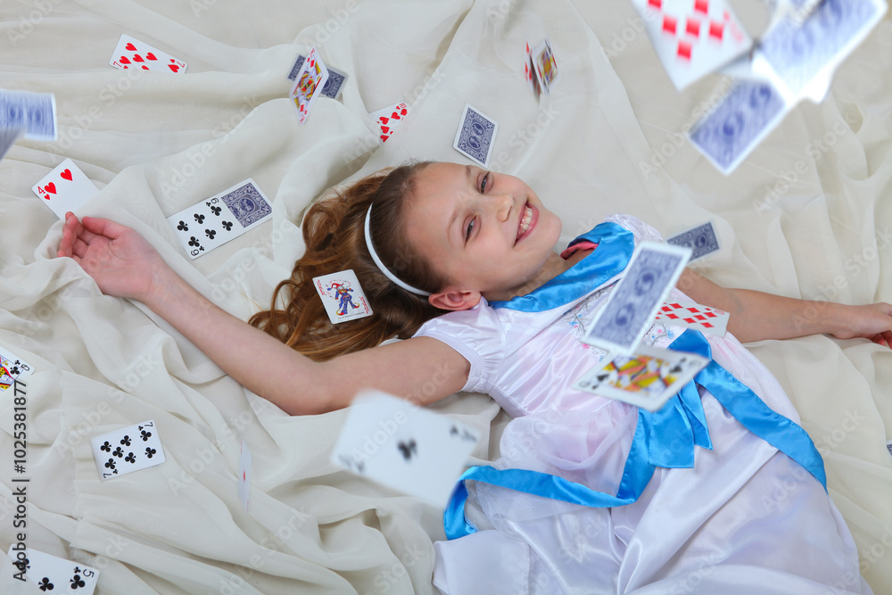 cheerful little girl in Alice in Wonderland costume lying down with ...