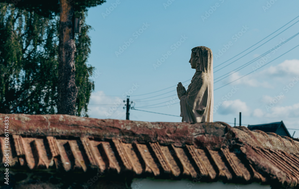 Stone statue of a woman in a long robe. She is in a prayerful pose ...