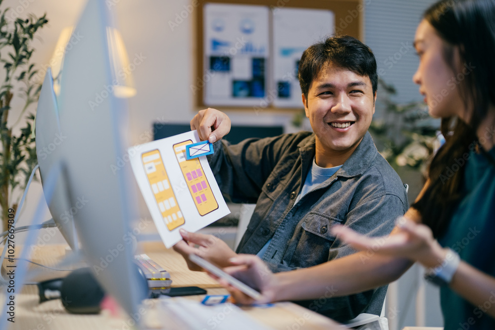 Two Asian Ui Ux Designers Collaborating On A Mobile App Wireframe In An Office Late At Night