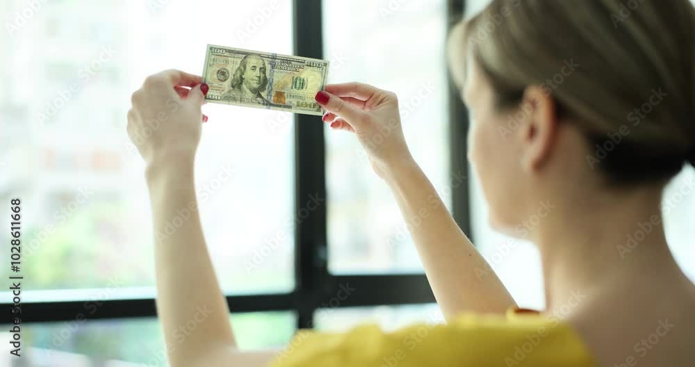 Checking counterfeit money and 100 dollars against window in hand ...
