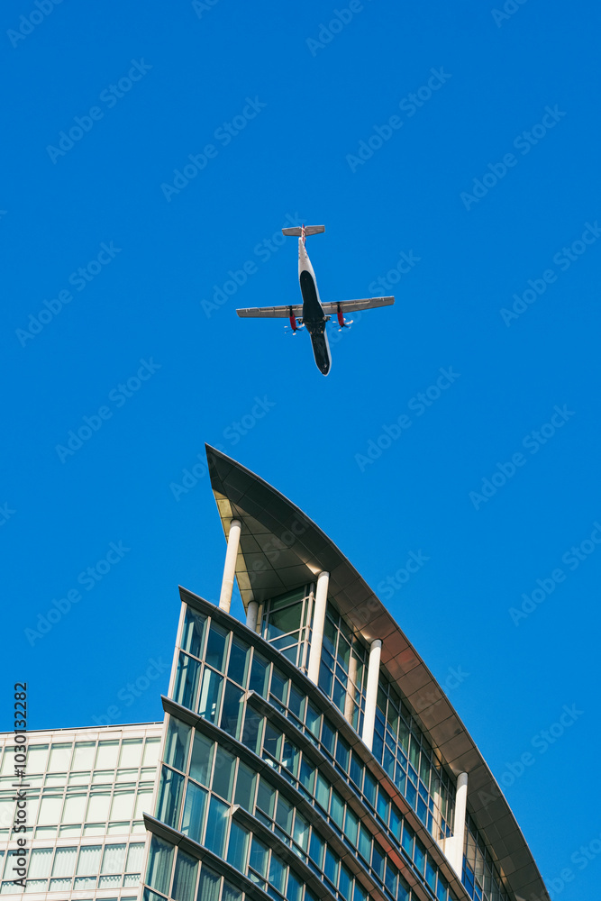 An airplane gracefully flies over a uniquely styled modern building ...