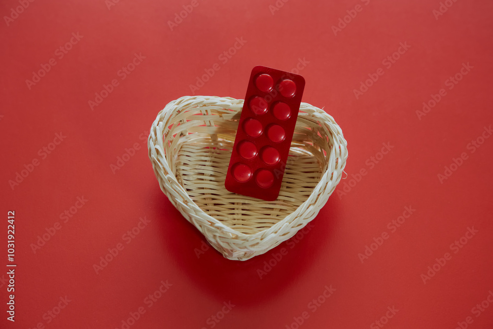 Heart shaped wicker basket with a blister of red pills in it on a red ...