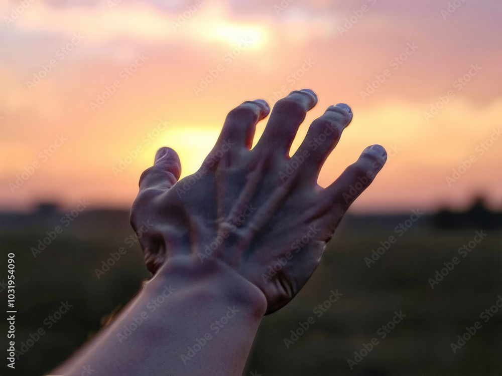 A hand is raised in the air with the sun in the background. The hand is ...